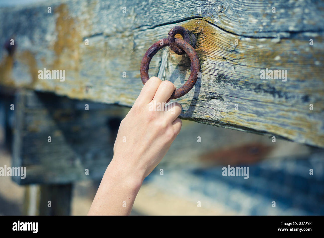 A young female hand is grabbing an old rusty chain attached to a wooden ...