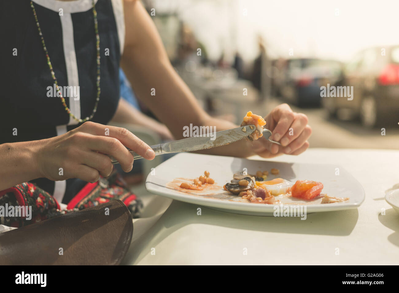 A young woman is having a traditional English breakfast at a table ...