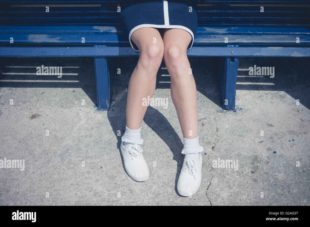 The legs and feet of a young woman sitting on a bench on a sunny day in ...