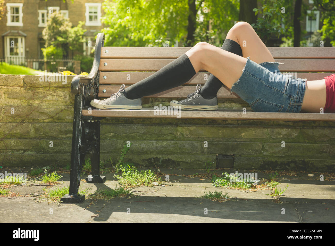 A young woman is lying down and relaxing on a park bench on a sunny ...