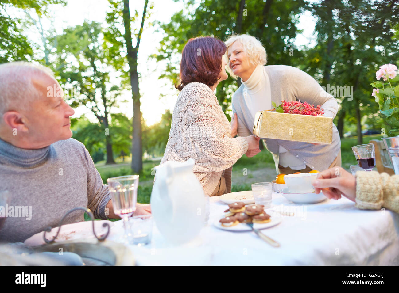 Senior congratulating woman with gift at her birthday party in a garden ...
