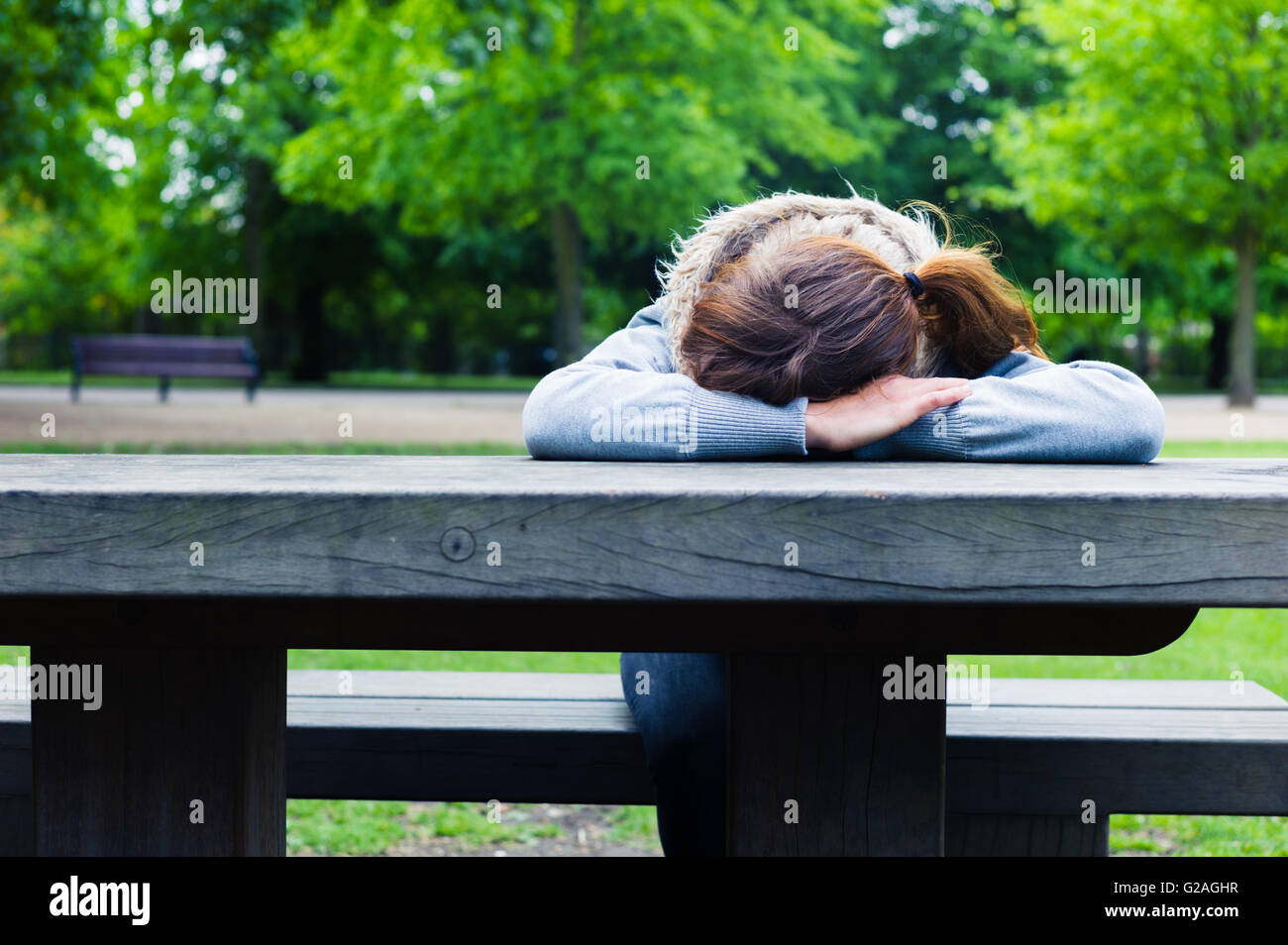 A sad young woman with her head resting on her hands at a table in the ...