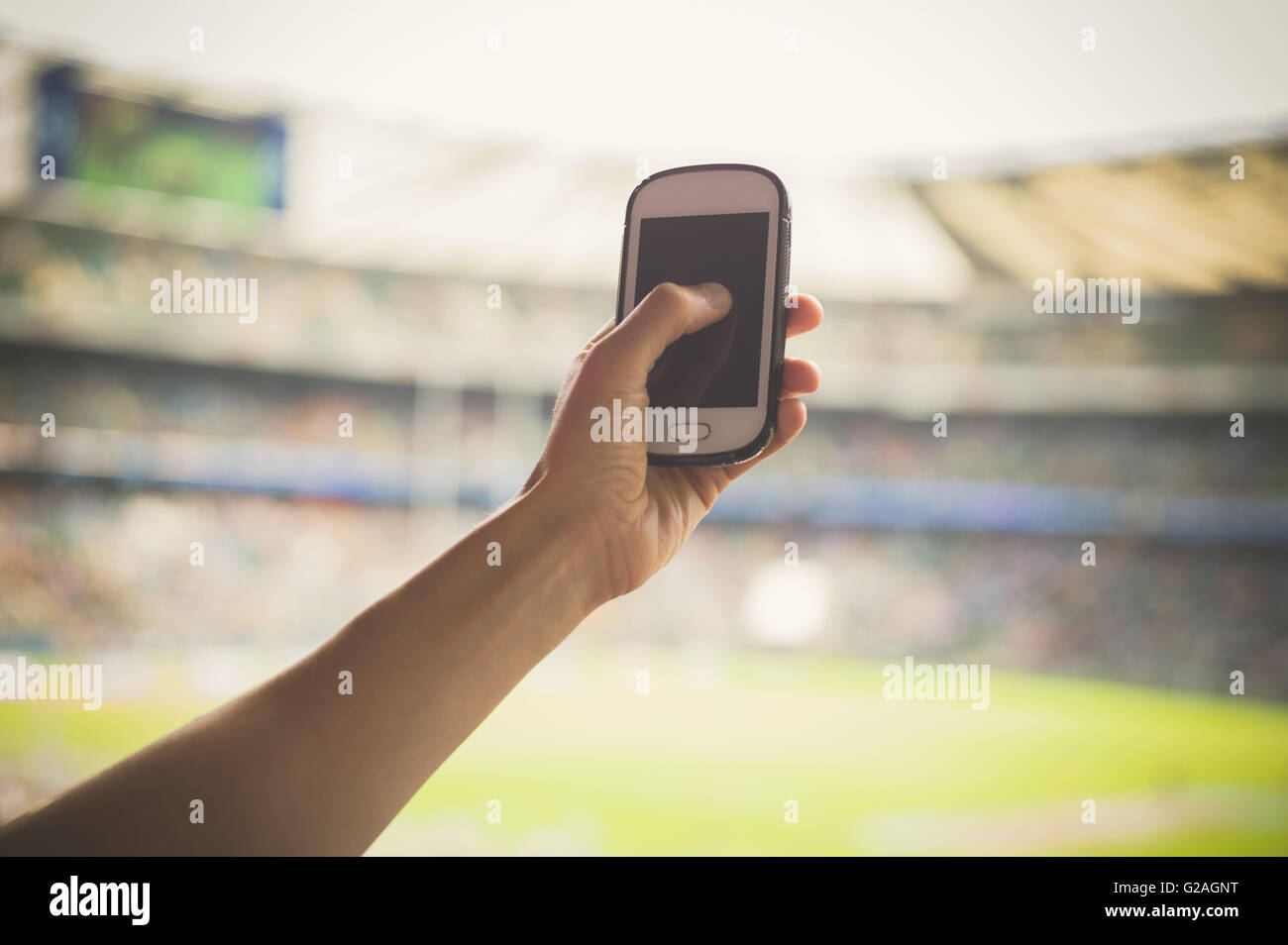 A female hand is holding a smart phone in a stadium to take pictures of ...