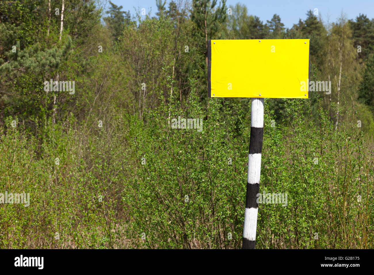 Empty yellow sign board on striped black and white pole over summer ...