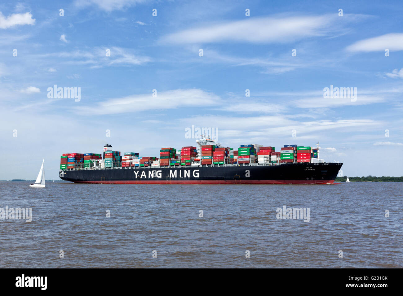 Ultra Large Container Ship YM Worth on the Elbe river near Hamburg. A small sail boat passing by ...
