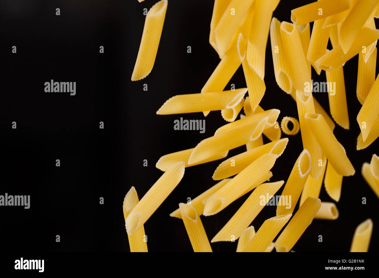 Falling penne pasta. Flying yellow raw macaroni over black background ...
