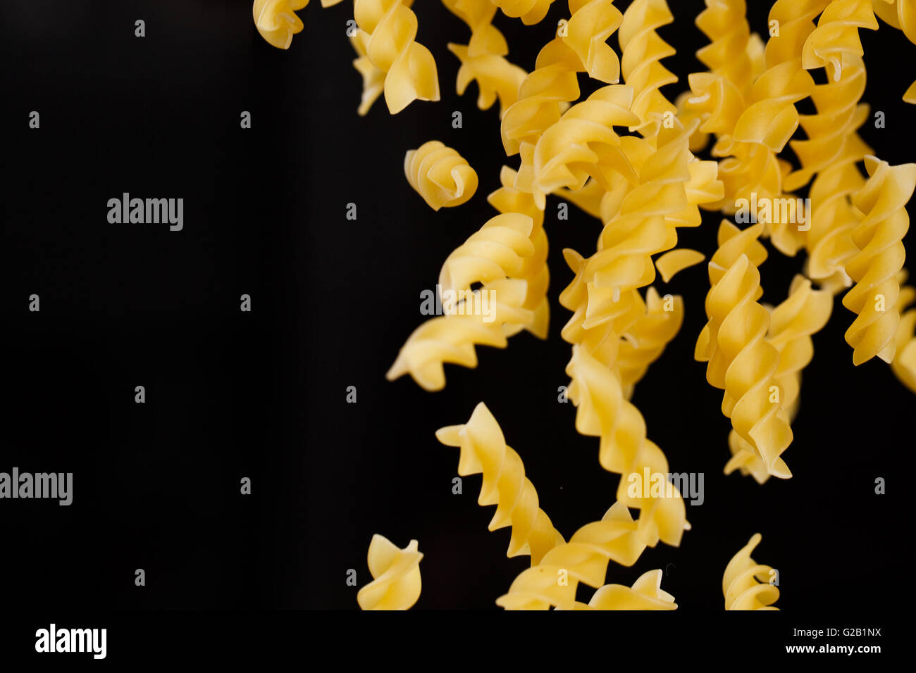 Falling fusilli pasta. Flying yellow raw macaroni over black background ...