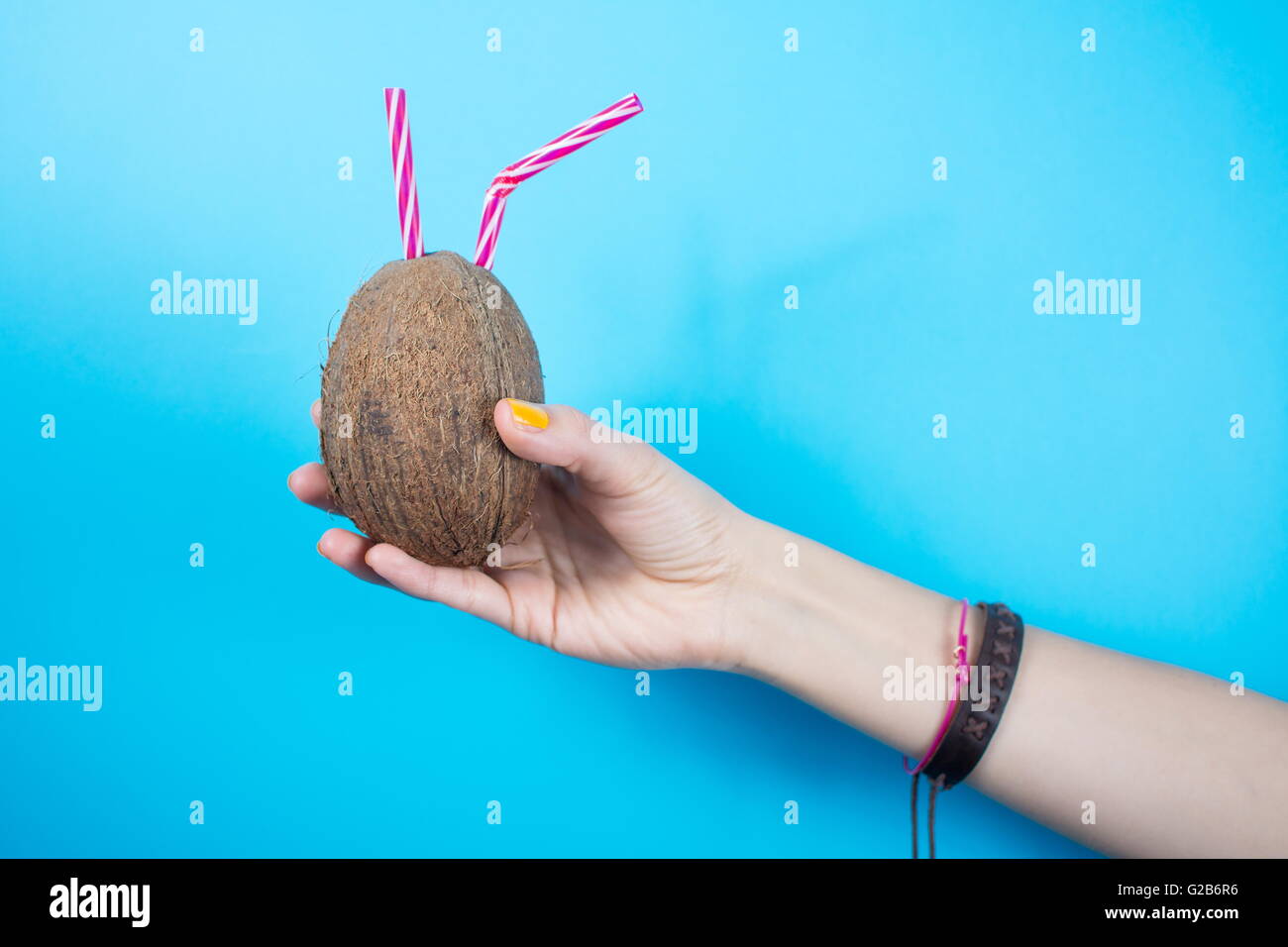 Womans hand holding a coconut with a straw against blue background ...