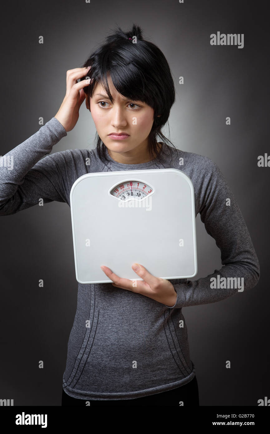 attractive fitness model, holding weighing scales, looking confused ...