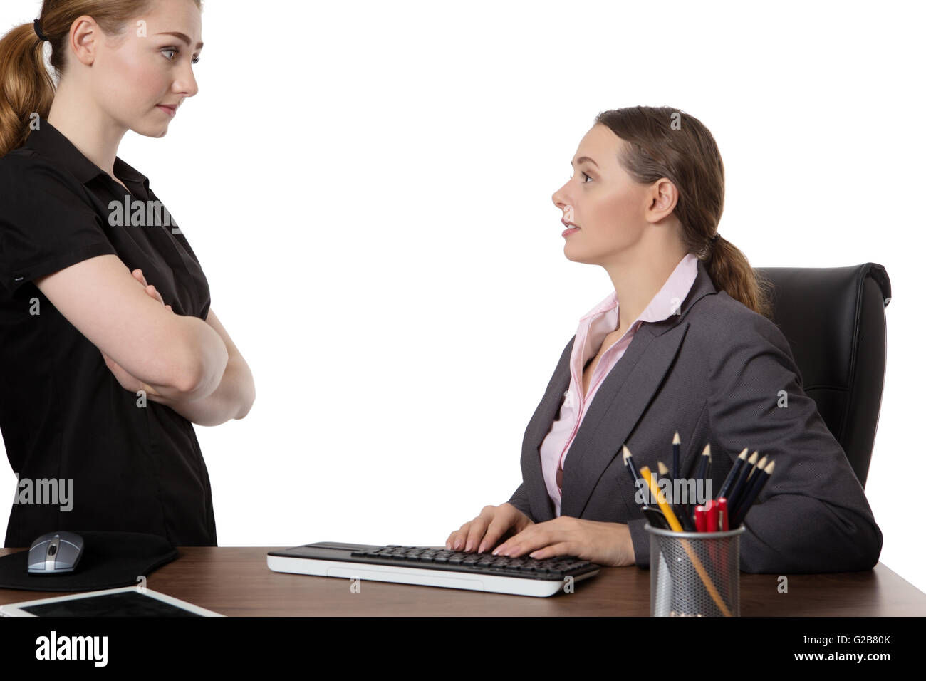 Two Young Female Co Workers In An Office One Sitting At A Desk