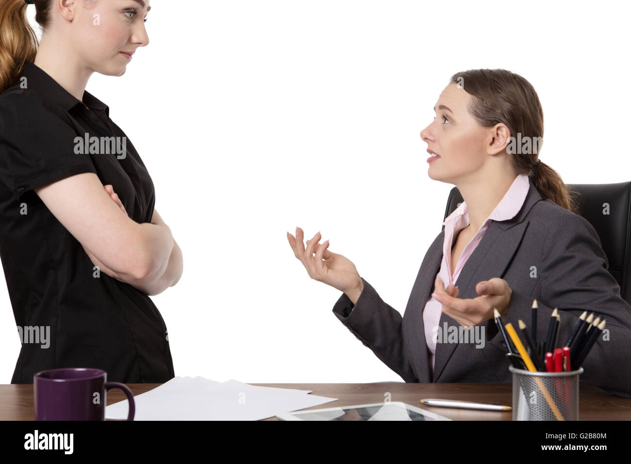 two young, female co-workers in an office. One sitting at a desk ...