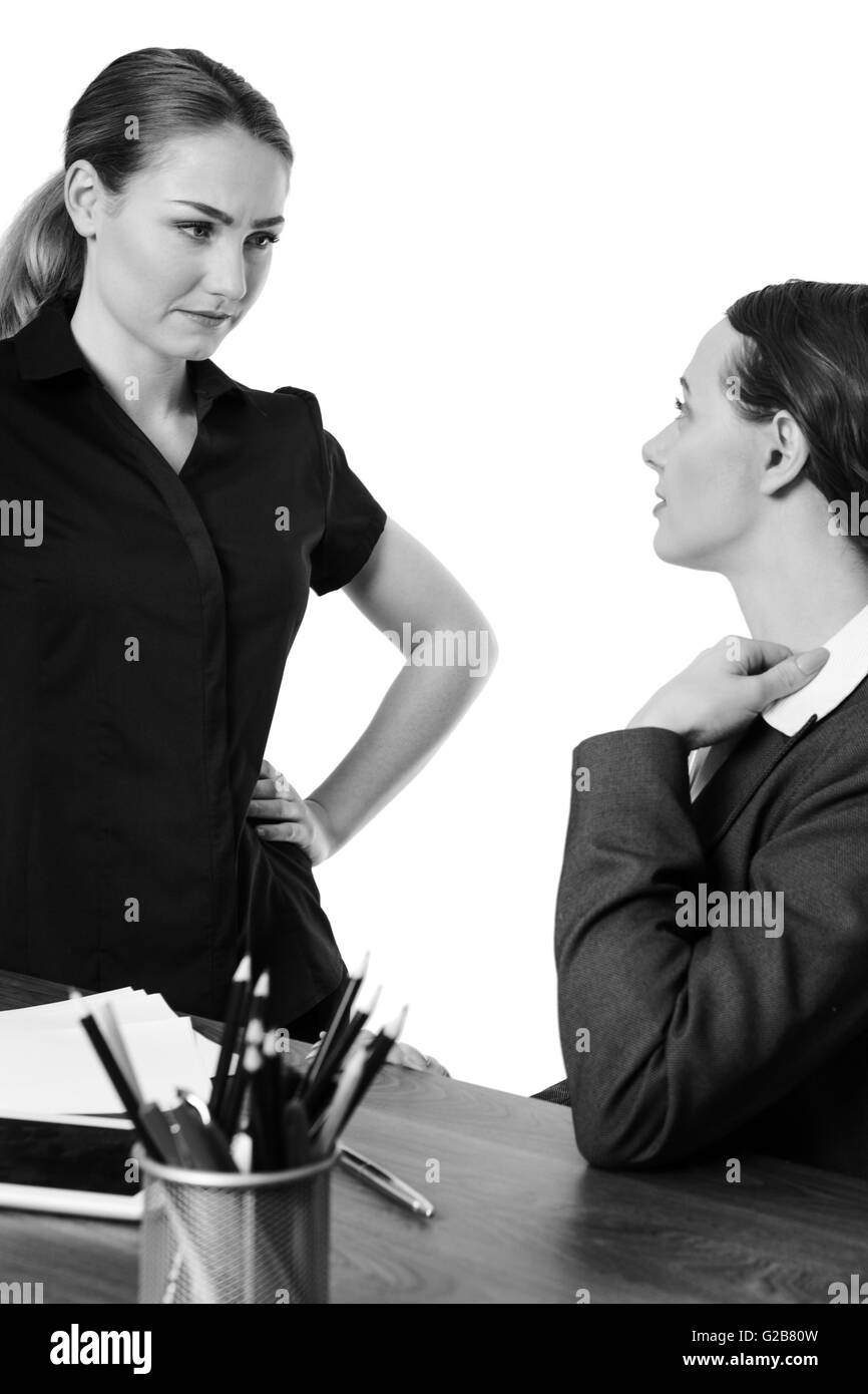 Two Female Co Workers In An Office One Sitting At A Desk Wearing A