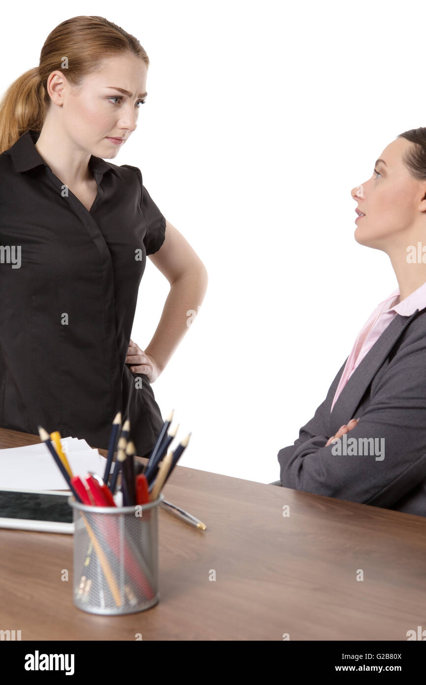 two female co-workers in an office. One sitting at a desk wearing a ...