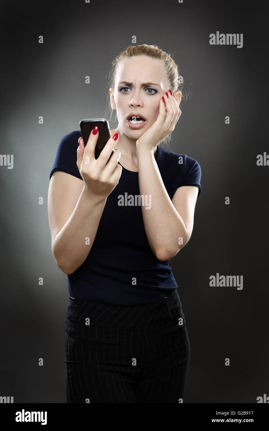 Pretty business woman is staring at her mobile phone in disbelief with ...