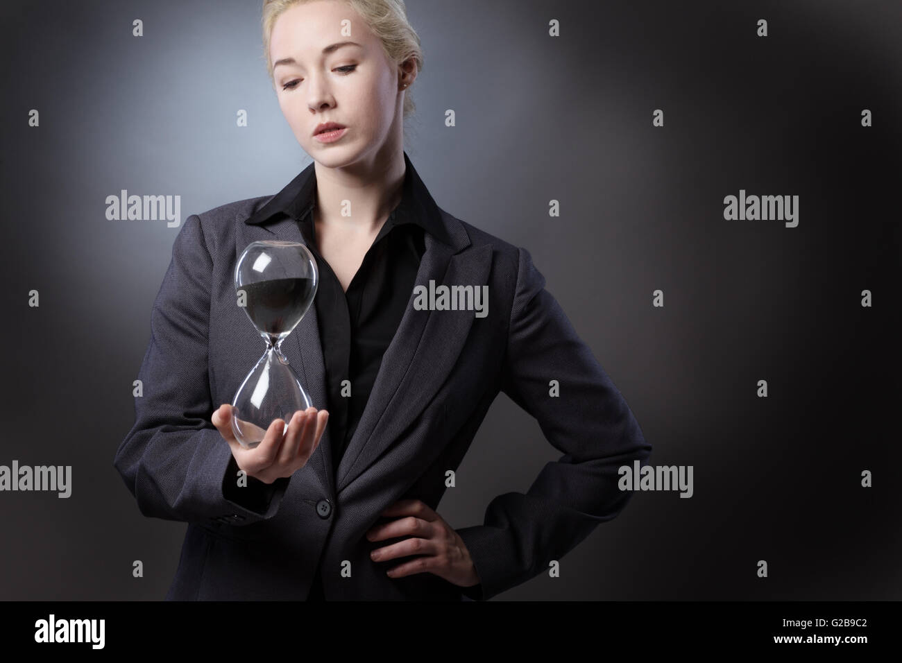 Studio shot of a woman in a suit holding a sand timer in her hands ...
