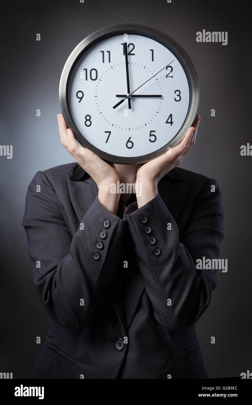 Business woman in a suit holding a large round numerical clock in front ...