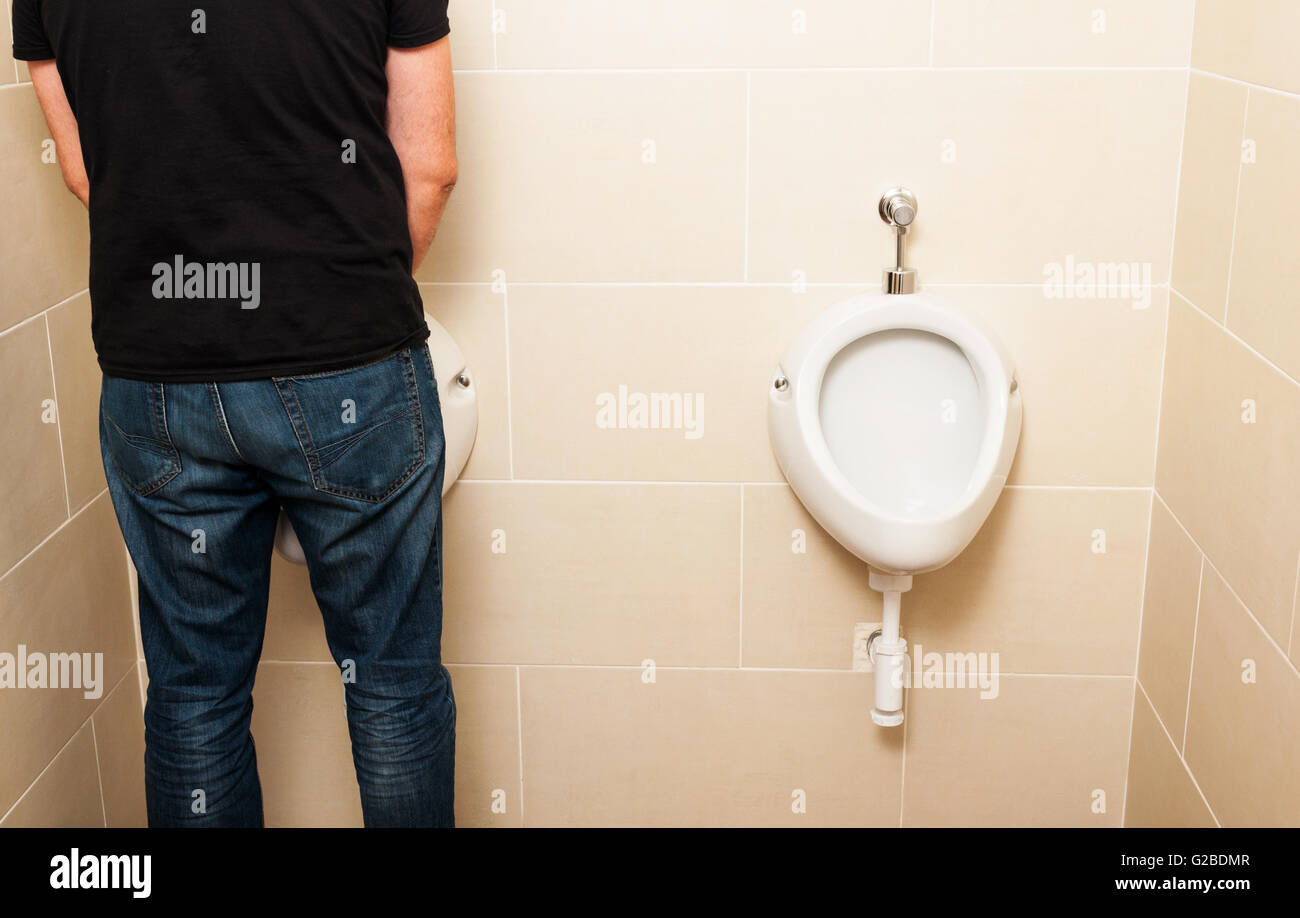 man standing in front of a white pissoir in a public modern bathroom ...