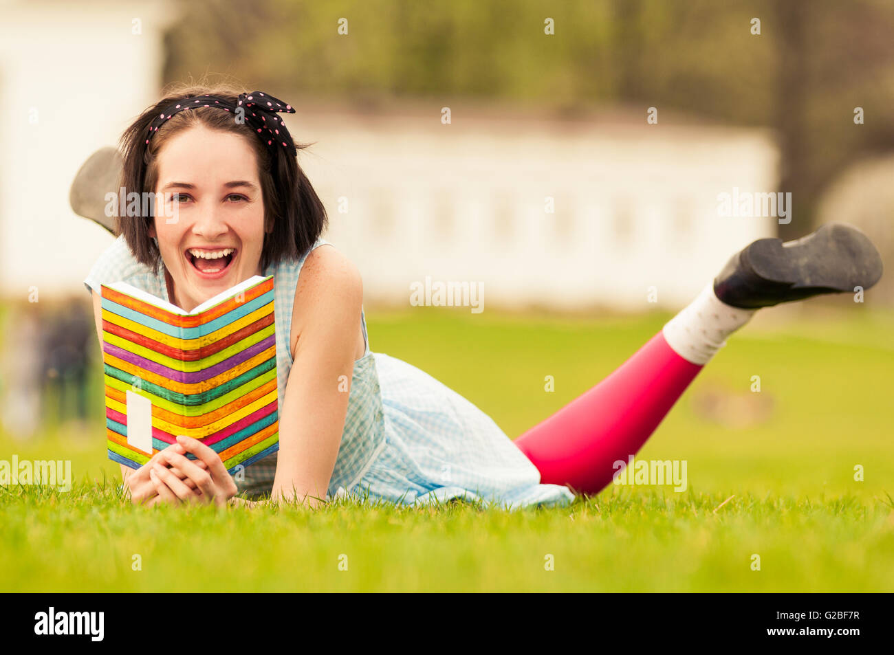 Portrait of beautiful smiling woman lying on grass reading book and ...