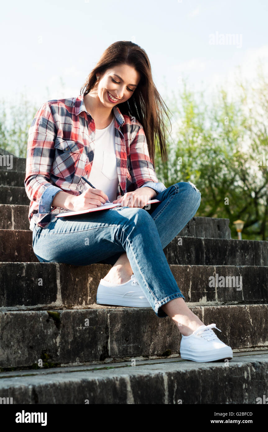 Cheerful female relaxing outside and writing in her diary in a sunny ...