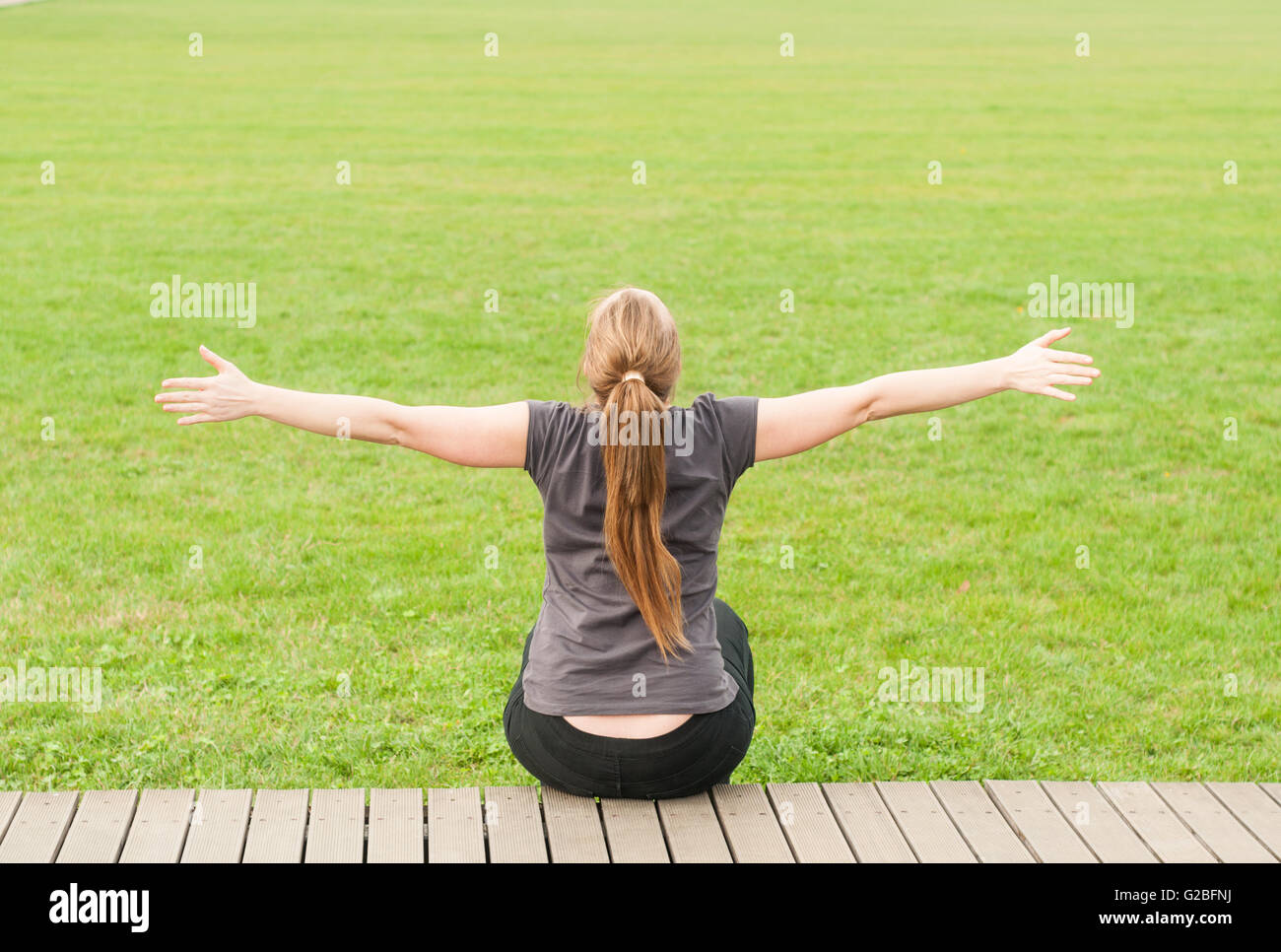 Young woman in back view sitting in the park with arms outstretched as ...