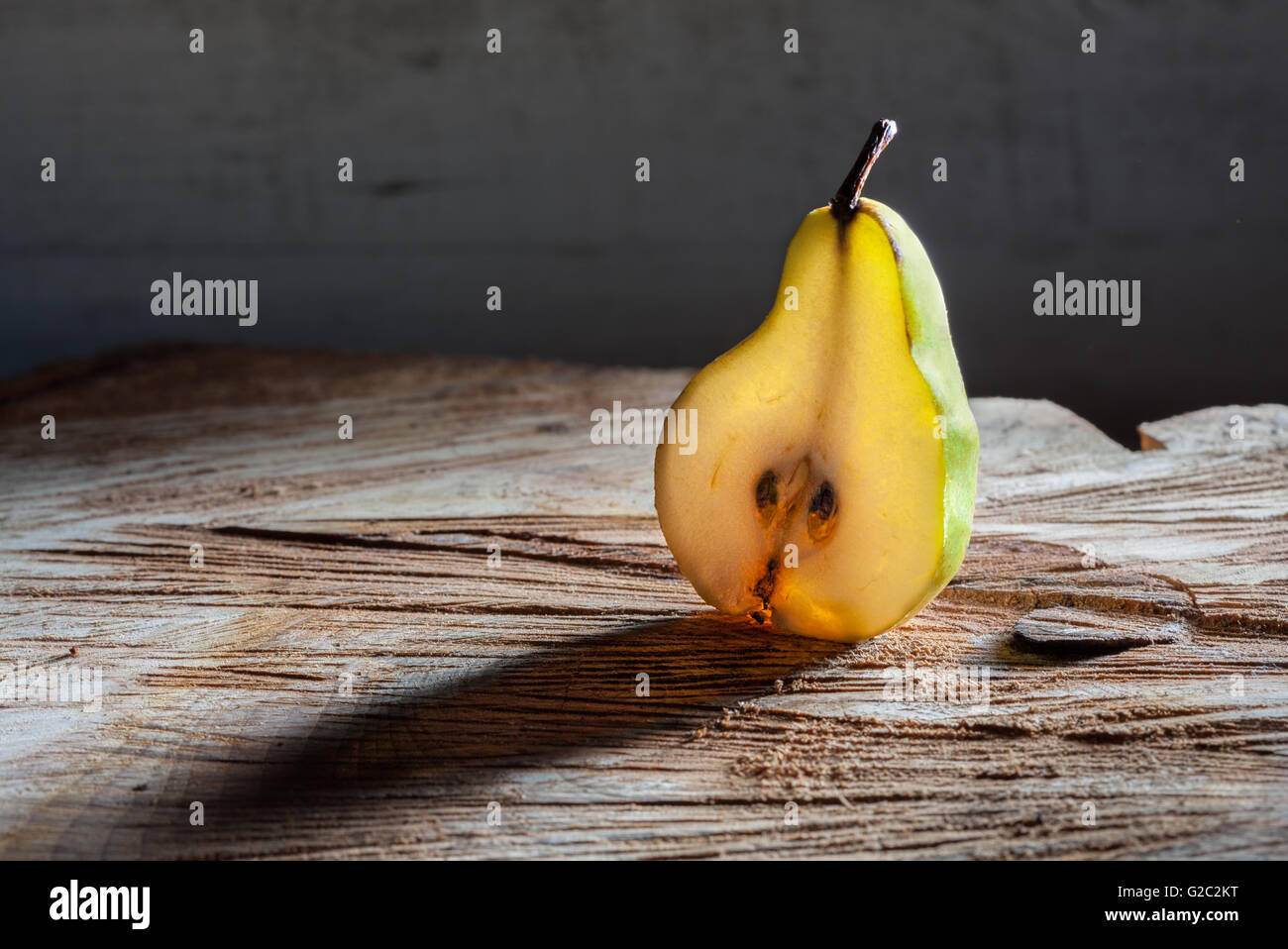 Half of pear glowing with back light on rough wooden surface with copy ...