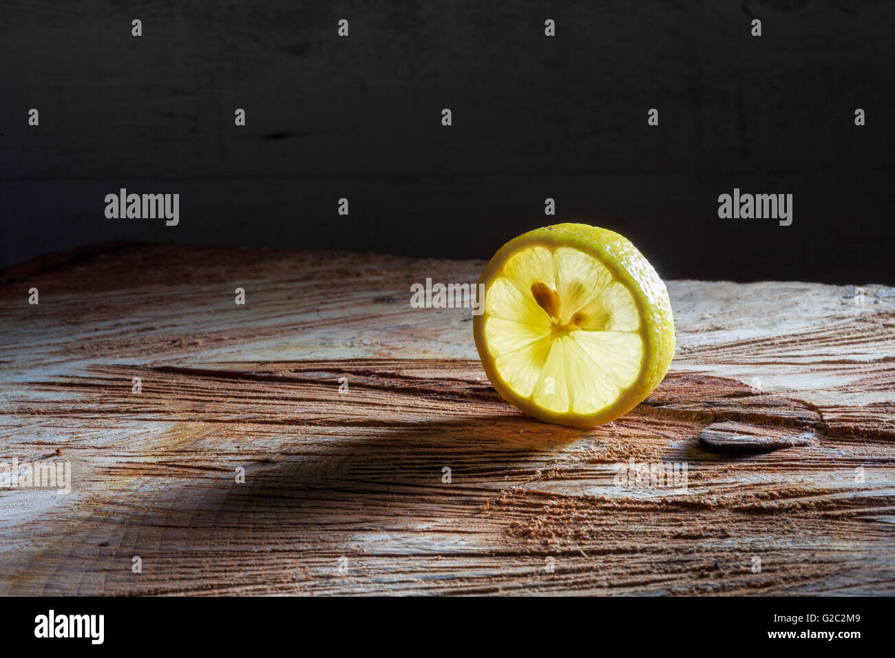 Slice of lemon glowing in translucent light on rough wooden surface ...