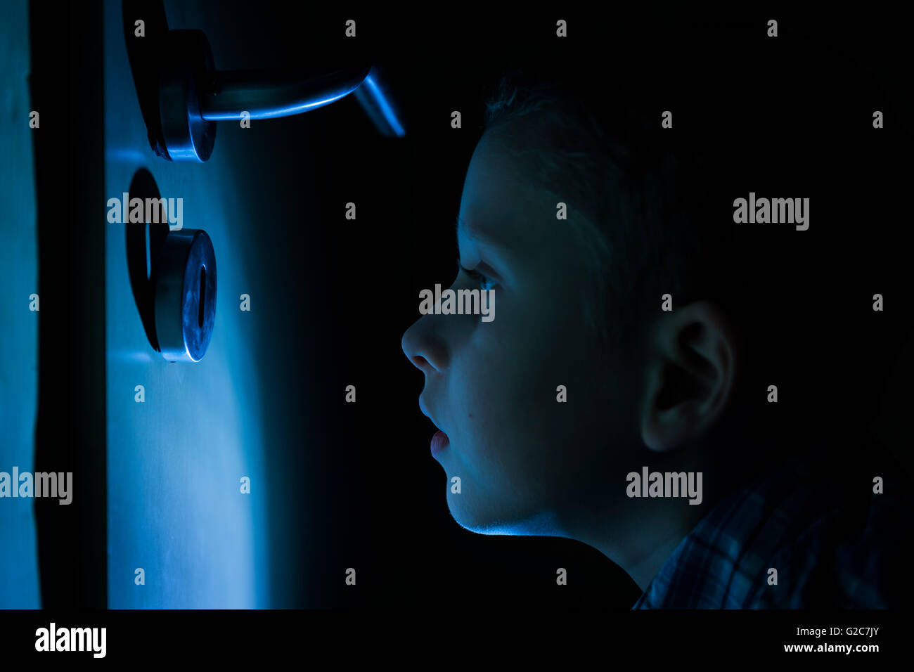 Boy in a dark room looking in the glow of flashlight through a Keyhole ...