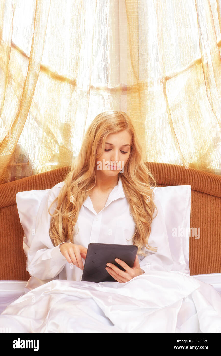 Young happy blonde woman in the bed browsing tablet computer Stock ...