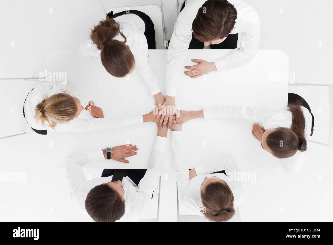 Businesspeople sitting around the table stacking hands one over each ...