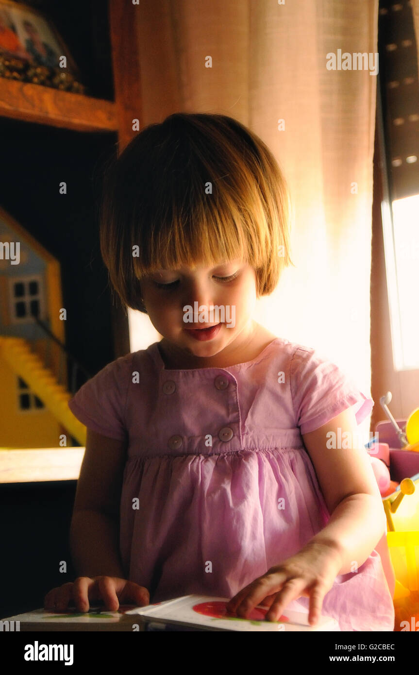 little girl watching an educational book on a table in a room backlit ...