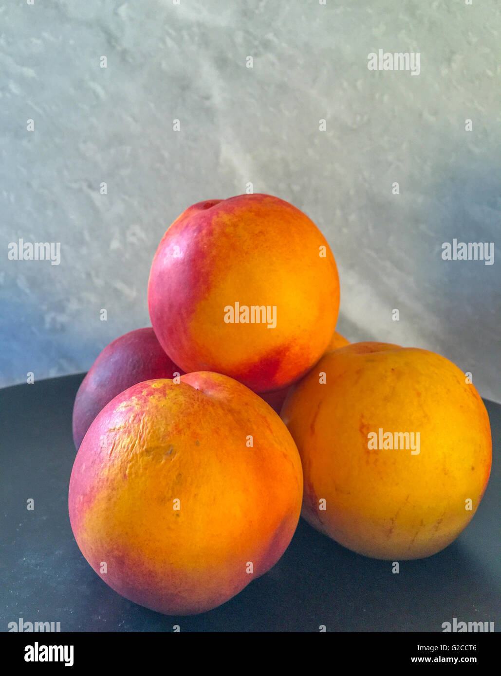 A still life of five peaches on a dark platter with marble in ...