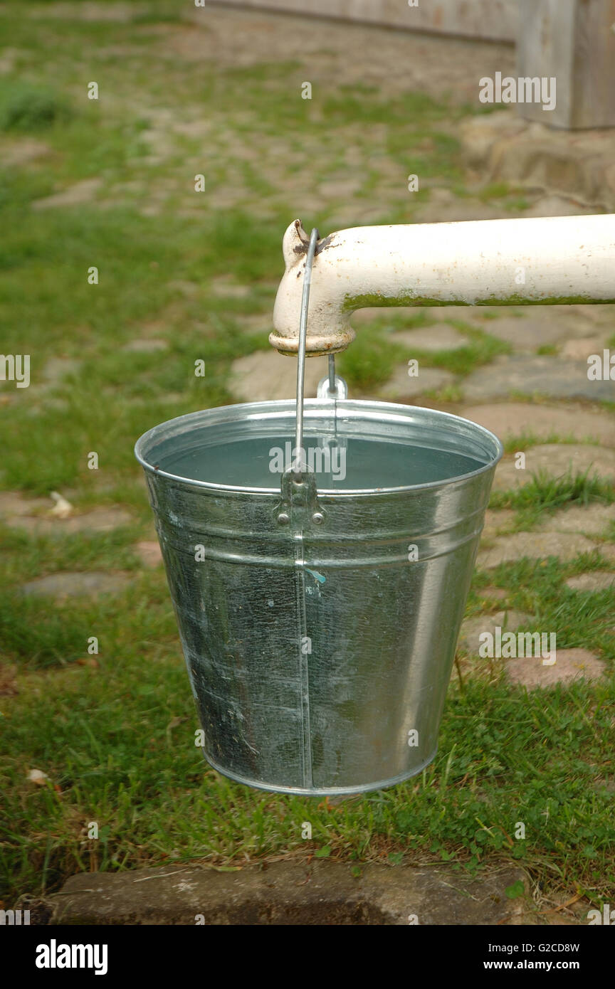 Silver bucket full of water hanging on pump Stock Photo - Alamy