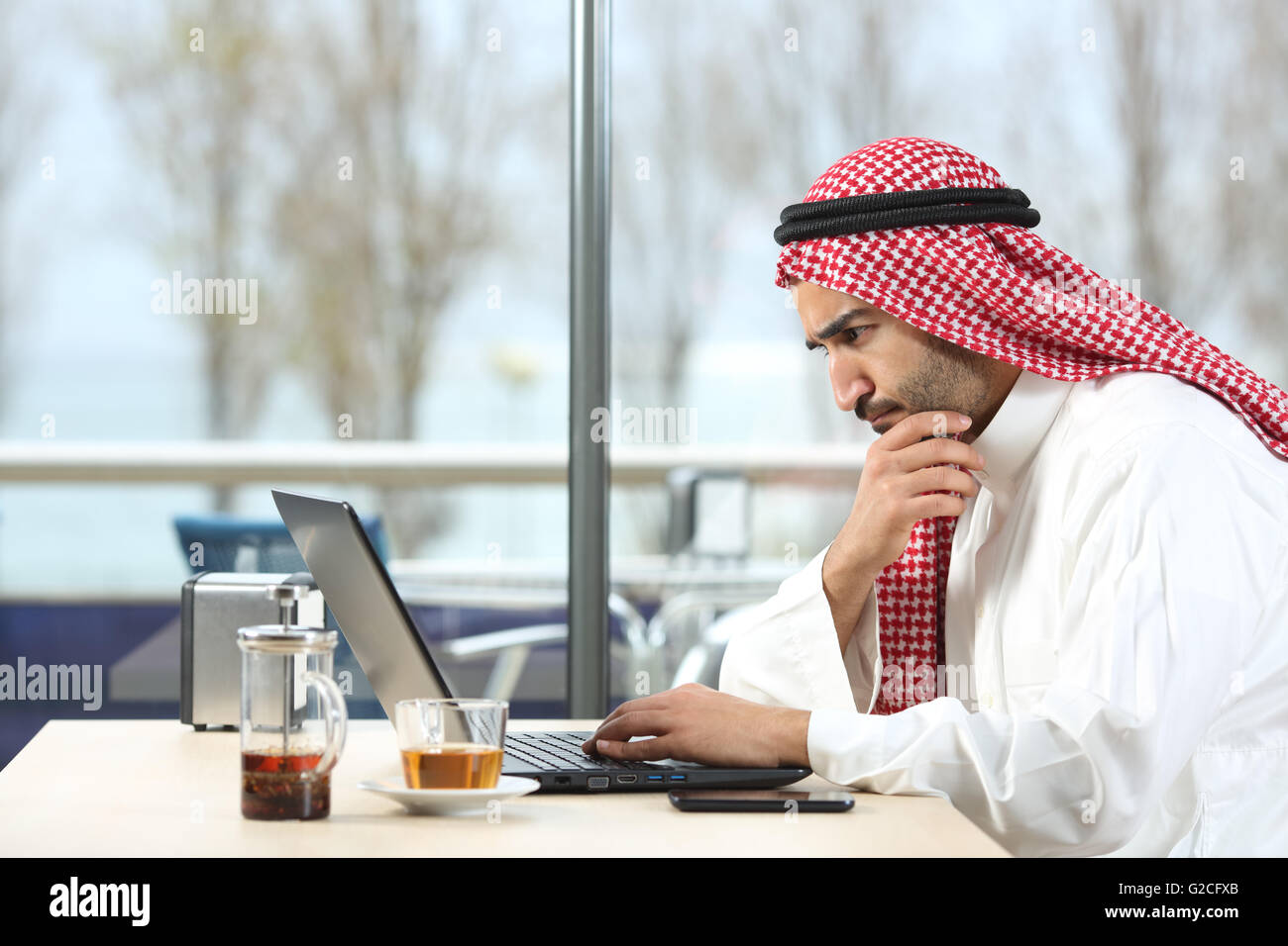 Side view of an arab saudi man worried working with a laptop in a ...