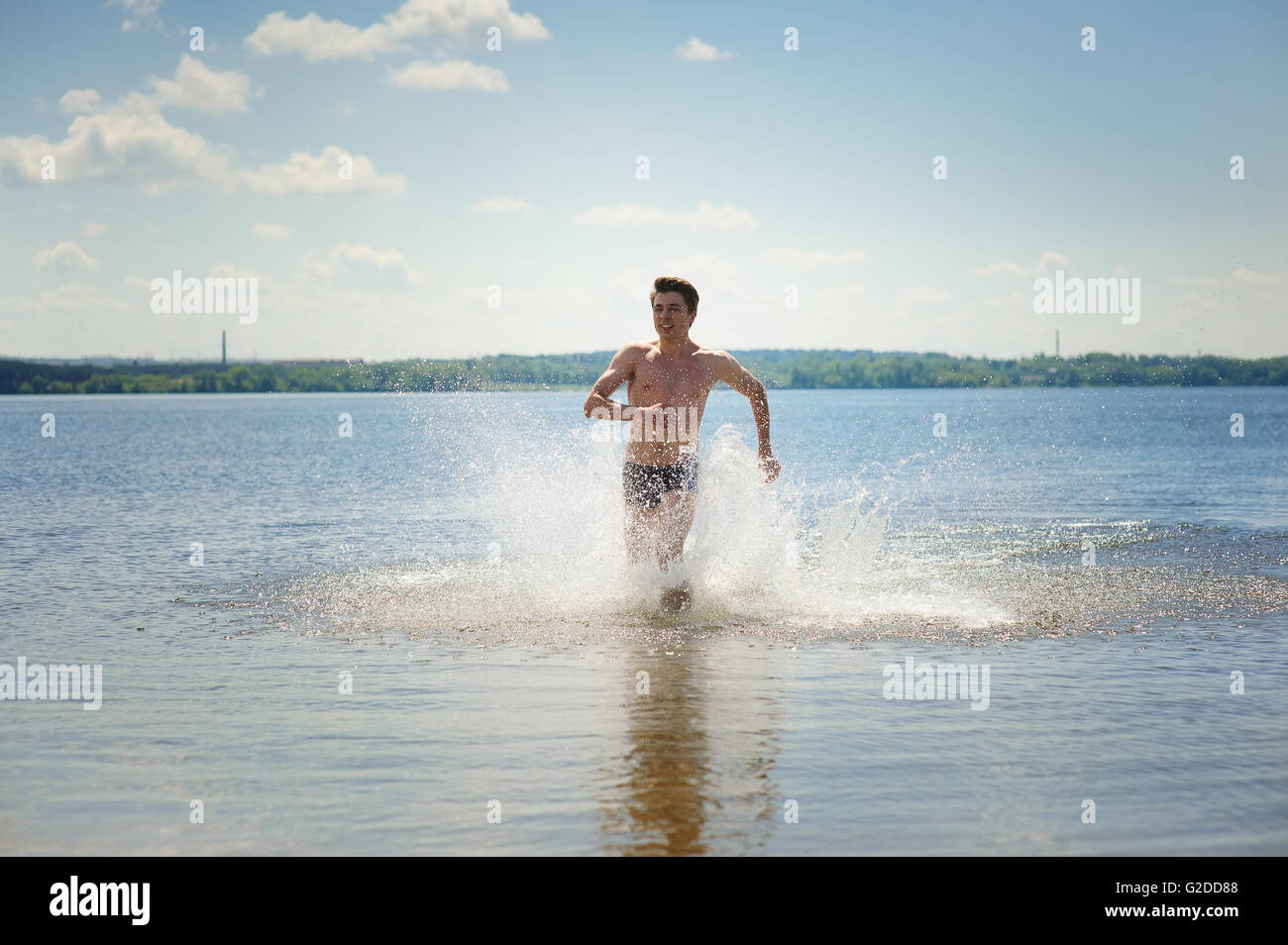 Man running through shallow water towards beach. Man is splashing water ...