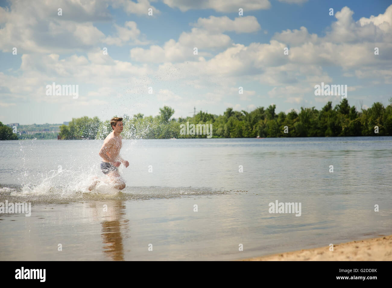 Man running through shallow water towards beach. Man is splashing water ...