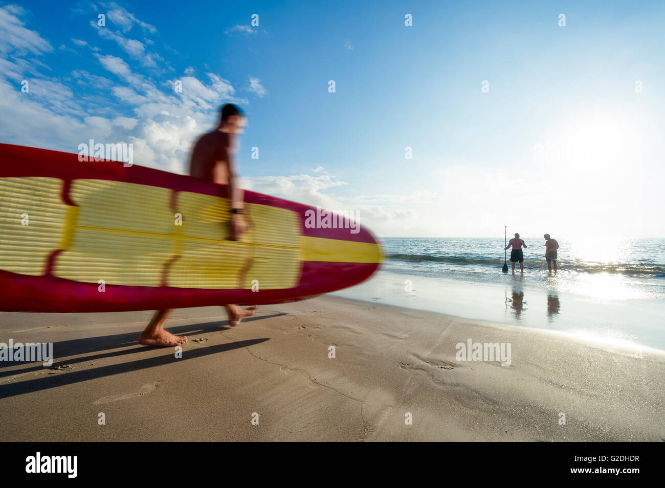 Motion blur of young Brazilian man carrying stand up paddle longboard ...