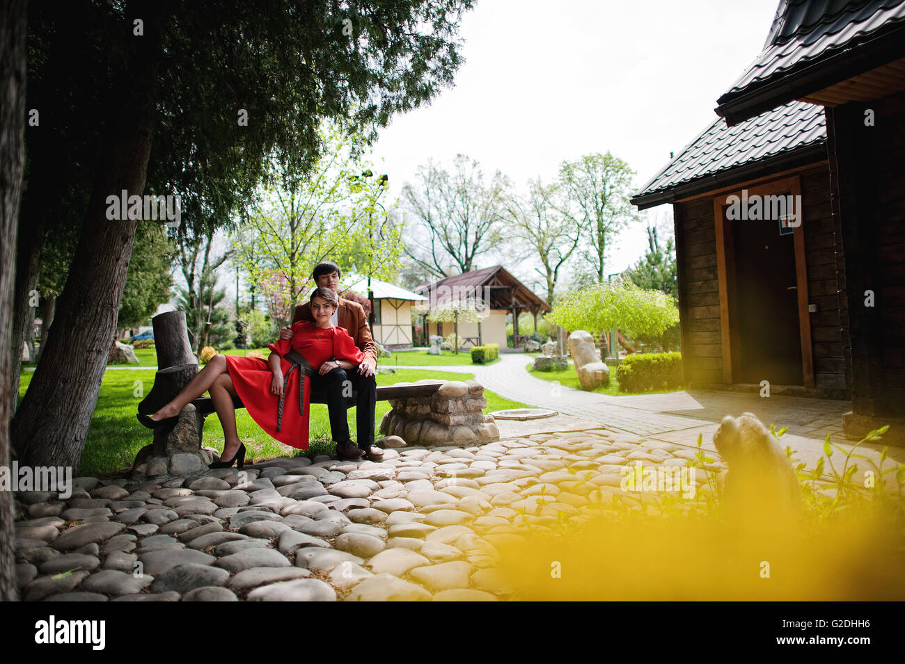 Couple sitting on bench. Stylish man at velvet jacket and girl in red ...