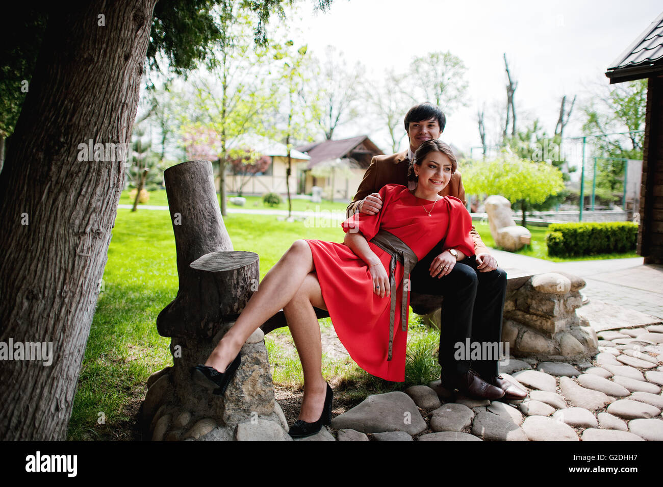 Couple sitting on bench. Stylish man at velvet jacket and girl in red ...