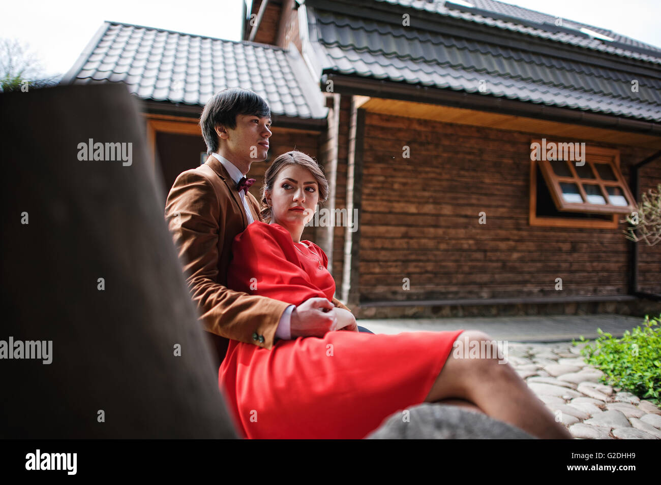 Couple sitting on bench. Stylish man at velvet jacket and girl in red ...