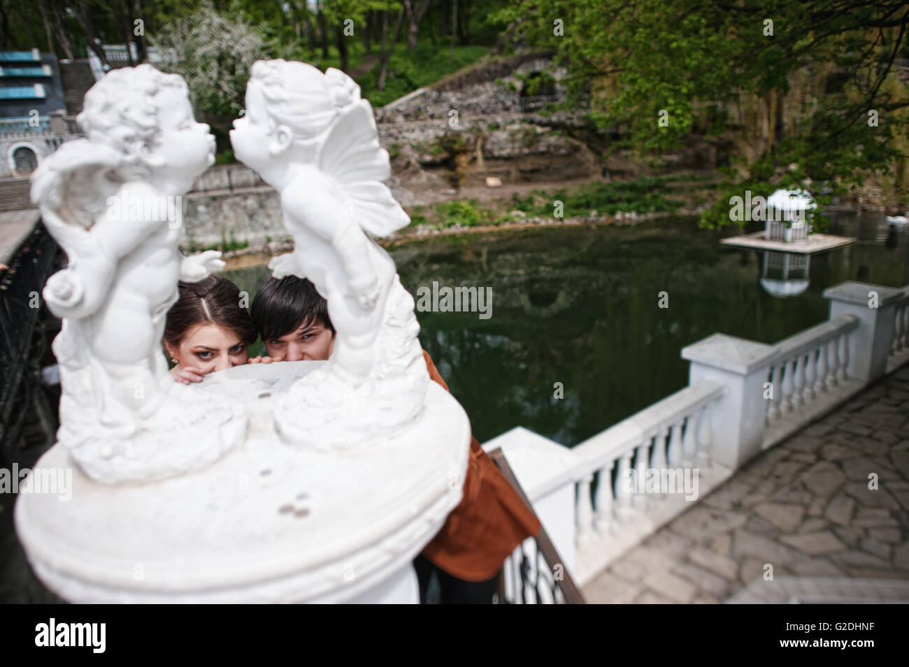 Couple hiding from statue of two kissing cupids angels Stock Photo - Alamy