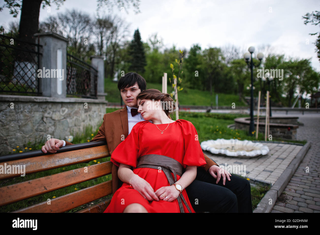 Couple lying on the bench. Stylish man at velvet jacket and girl in red ...