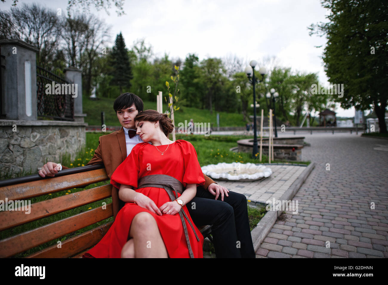 Couple lying on the bench. Stylish man at velvet jacket and girl in red ...