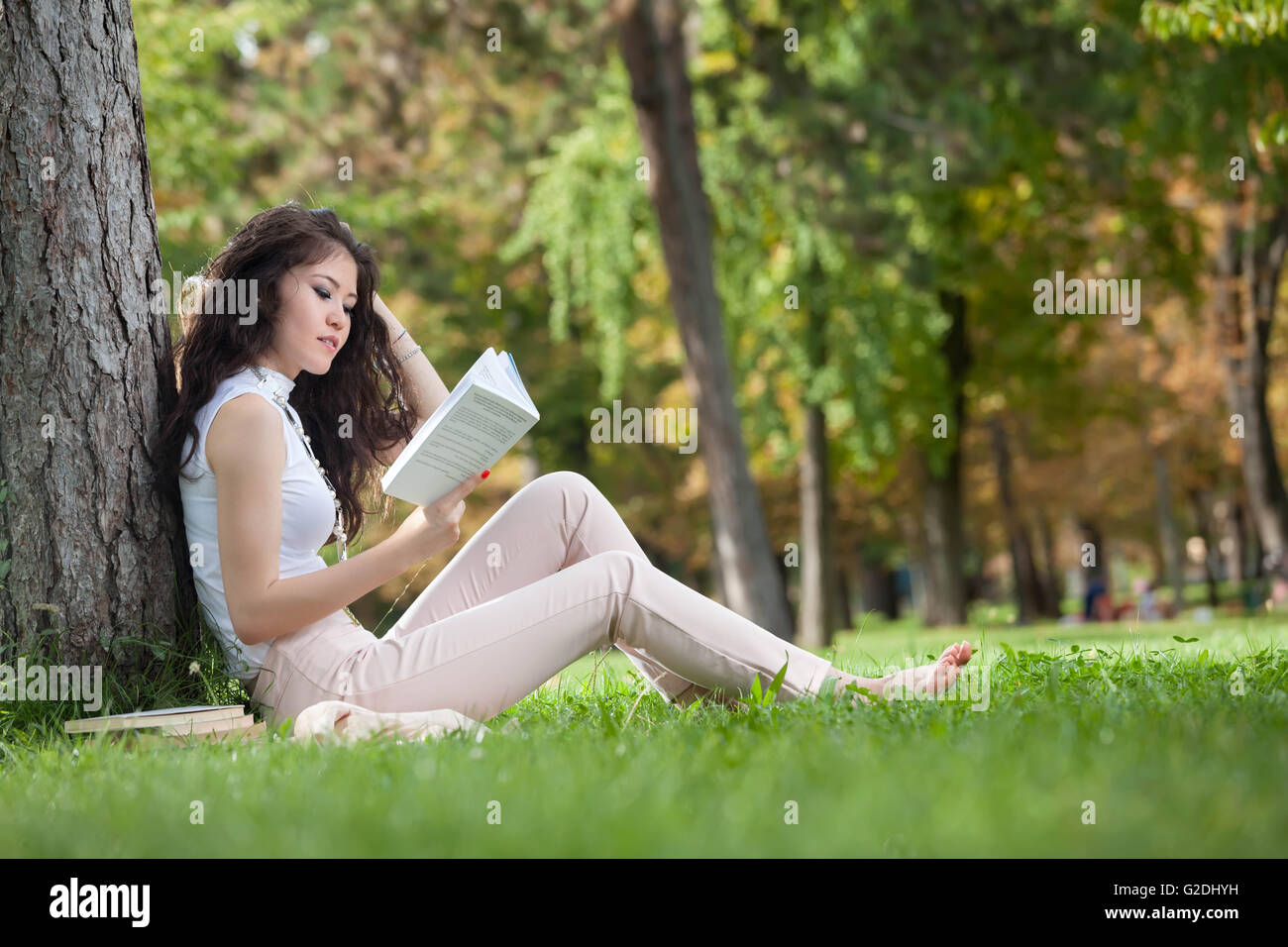 Young woman asian leaning against a tree and sitting in the grass ...