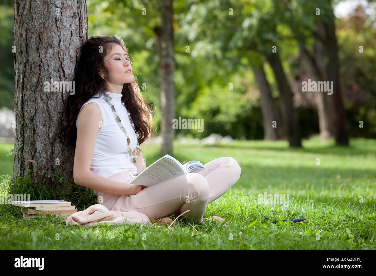 Young woman asian dreaming laying against a tree sitting in the grass ...