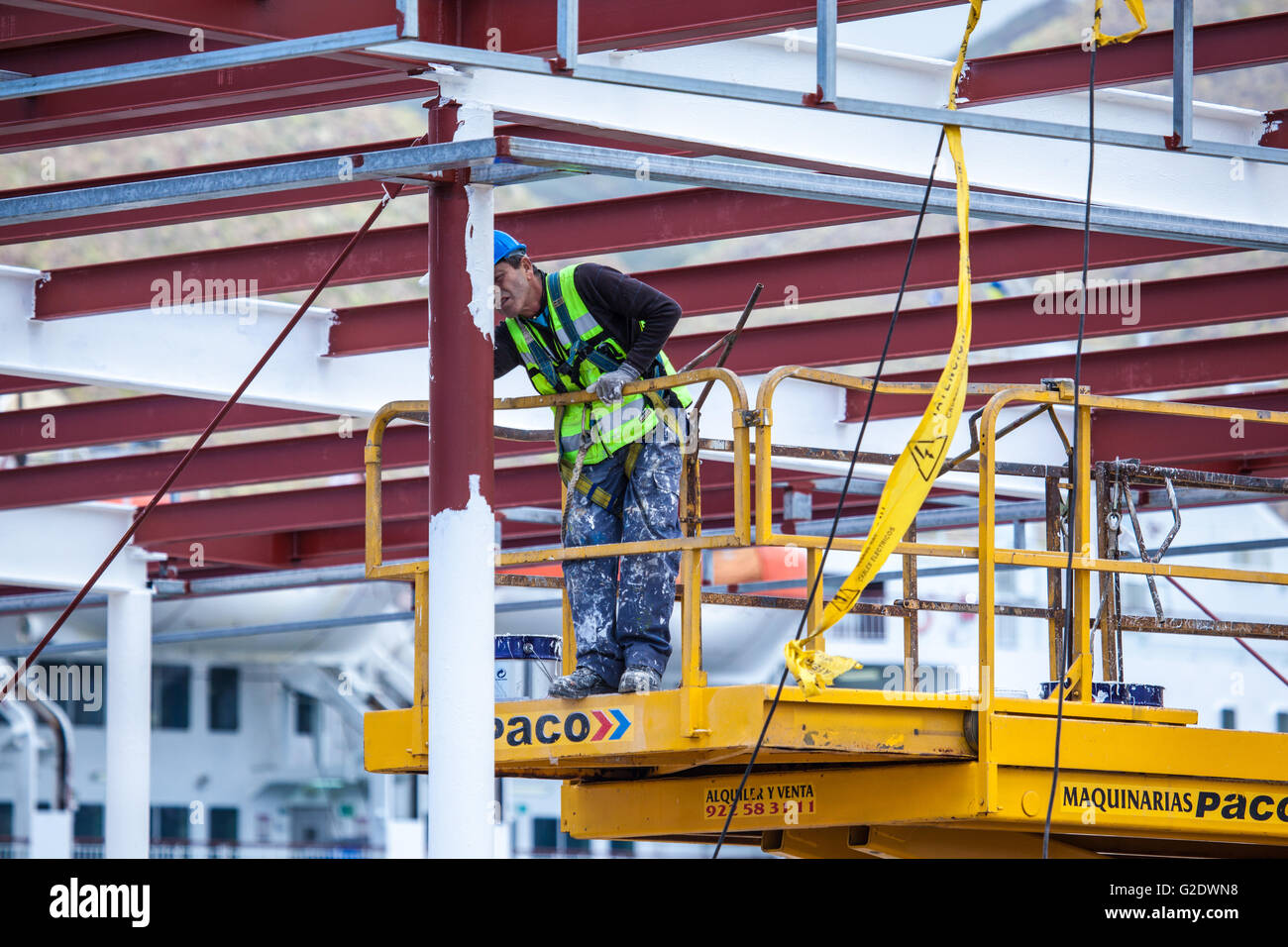 male painter working on a yellow lifting work platform beside a dock in ...