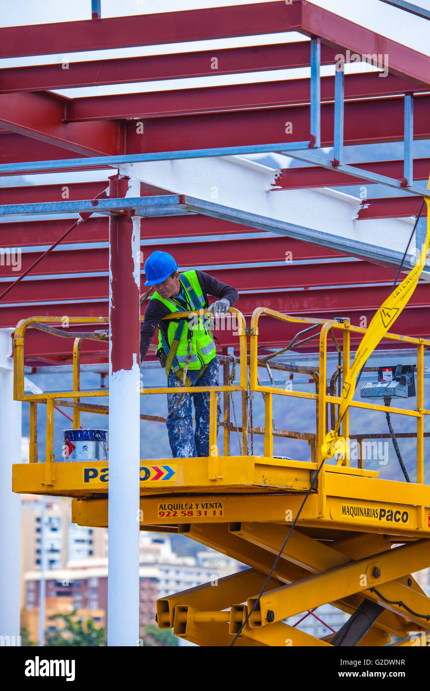 male painter working on a yellow lifting work platform beside a dock in ...