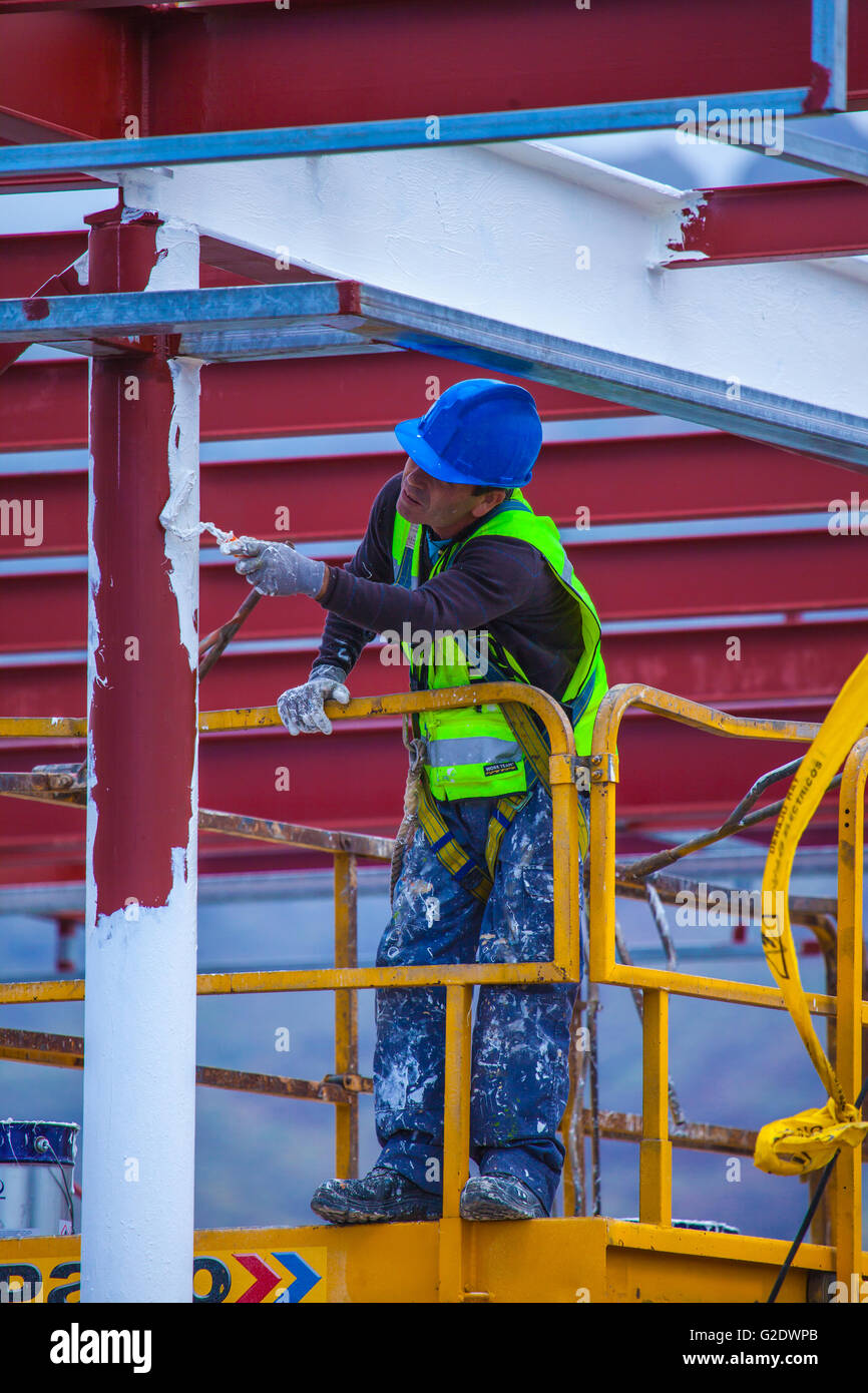 male painter working on a yellow lifting work platform beside a dock in ...