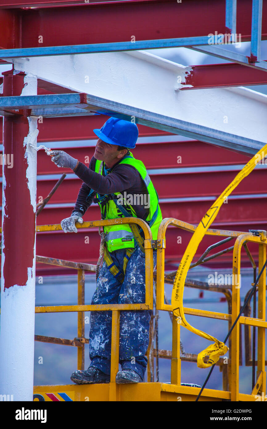 male painter working on a yellow lifting work platform beside a dock in ...