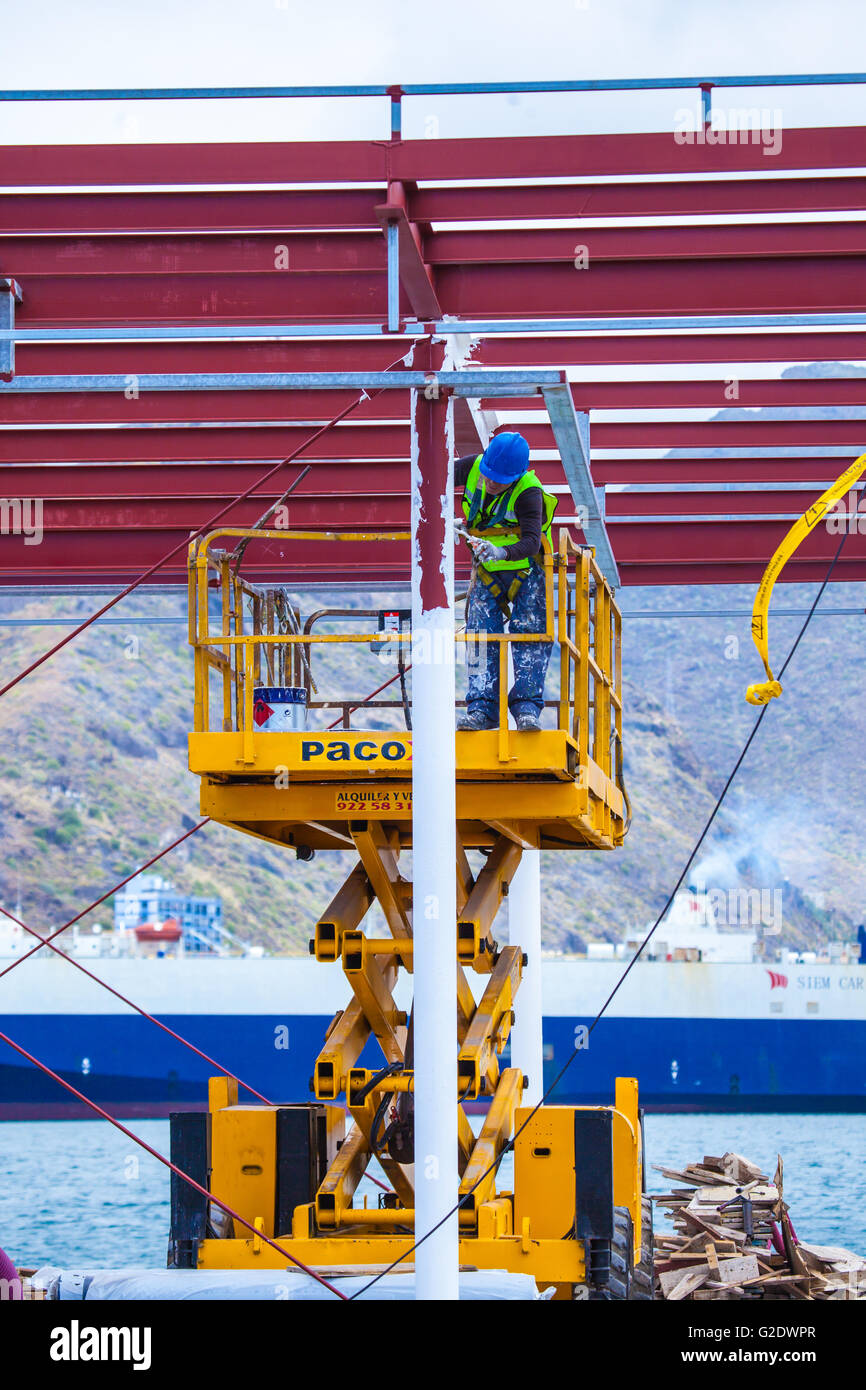 male painter working on a yellow lifting work platform beside a dock in ...