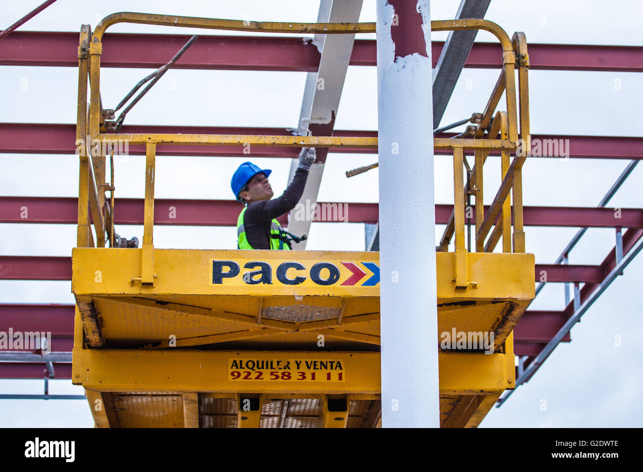 male painter working on a yellow lifting work platform beside a dock in ...
